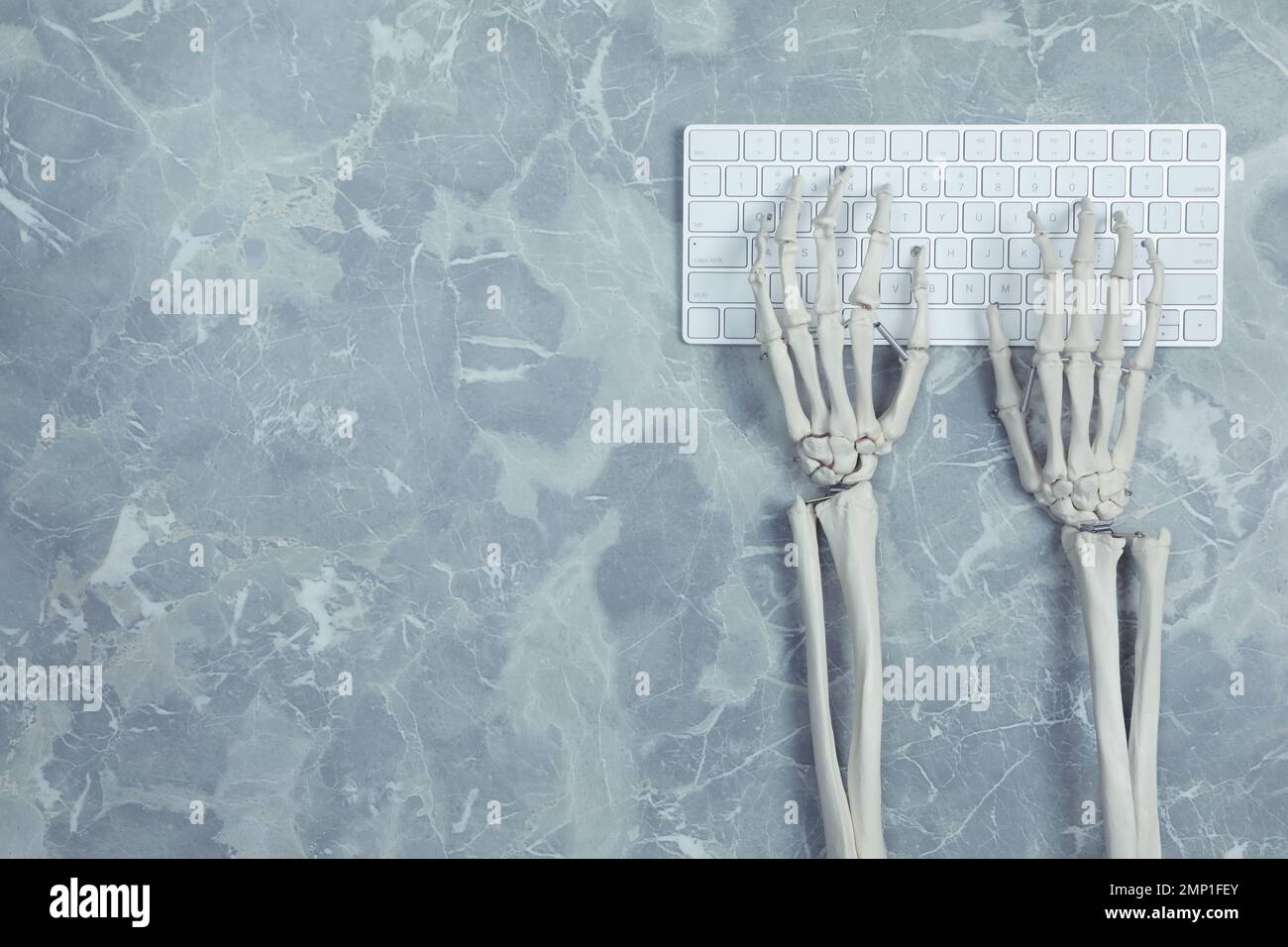 Human skeleton using computer keyboard at grey marble table, top view ...