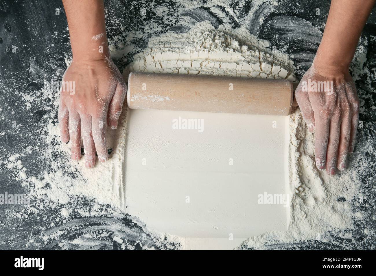 Baker rolling white flour with pin on dark table, closeup. Space for ...