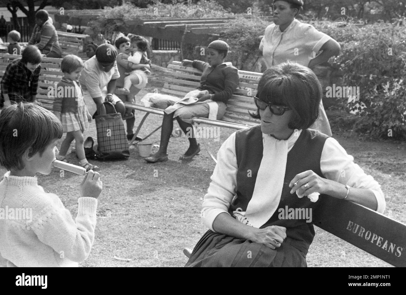 A housewife, seated on a European only bench, chats with her daughter ...