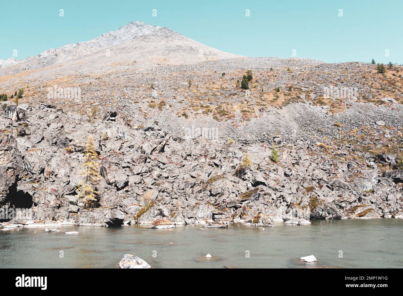 The sharp peak of a triangular stone mountain next to the water of a ...
