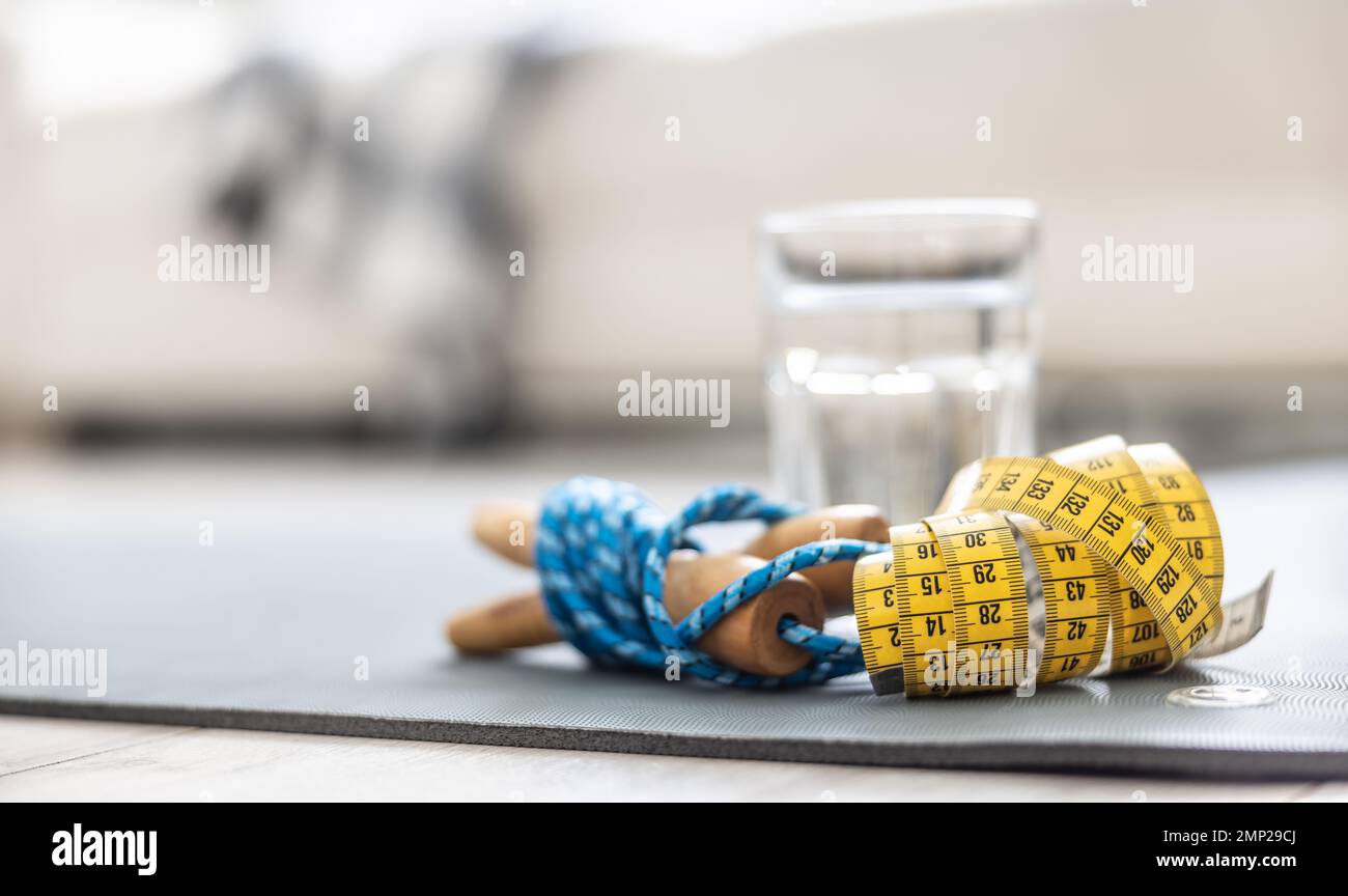 A skipping rope, a tape measure and a glass of water on a mat at home ...