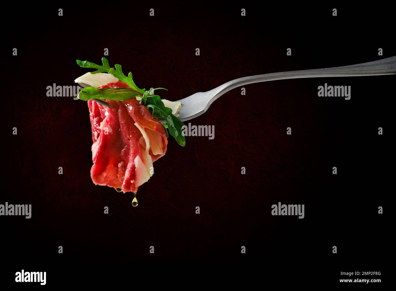 Piece of marbled beef carpaccio on fork with dripping olive oil over ...