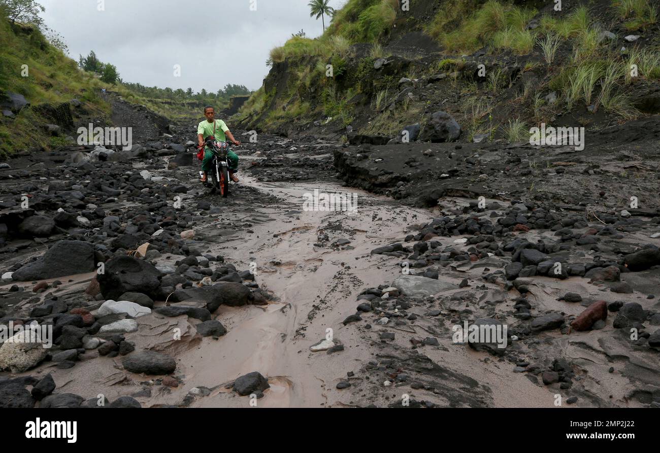 An evacuee drives his motorcycle through a gully which shows signs of lahar flow (volcanic ...
