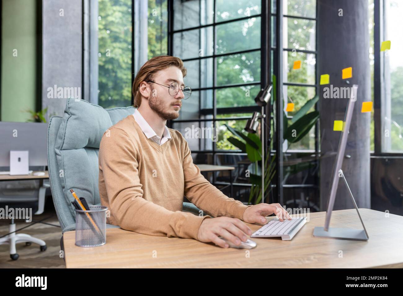 Young serious thinking businessman at work inside office with computer ...