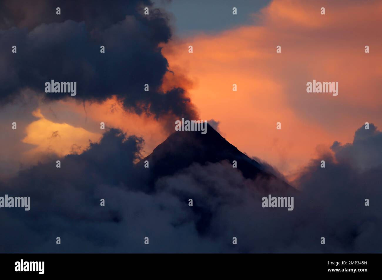 Mayon volcano emits ash during its mild eruption at sunset, as seen ...