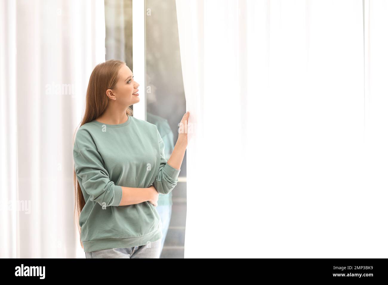 Beautiful young woman looking out of window at home Stock Photo - Alamy
