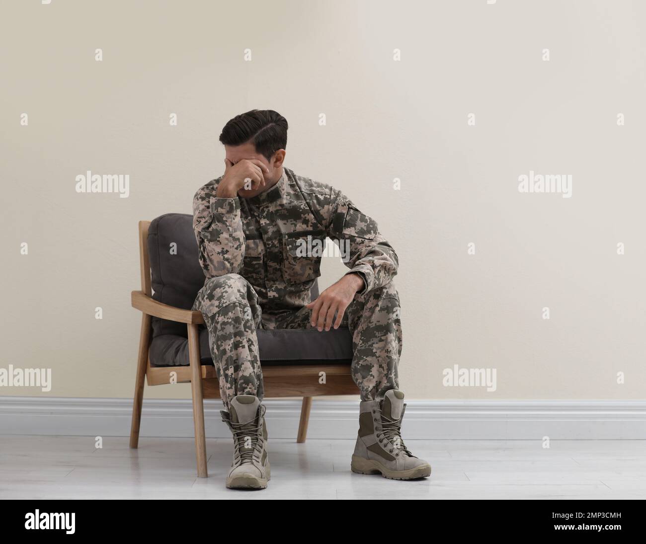 Stressed military officer sitting in armchair near white wall indoors ...