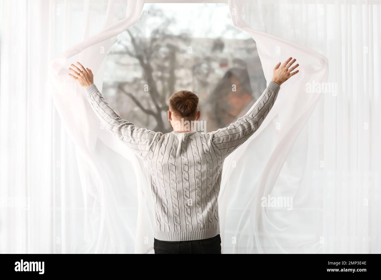 Young man opening window curtains at home, back view Stock Photo - Alamy