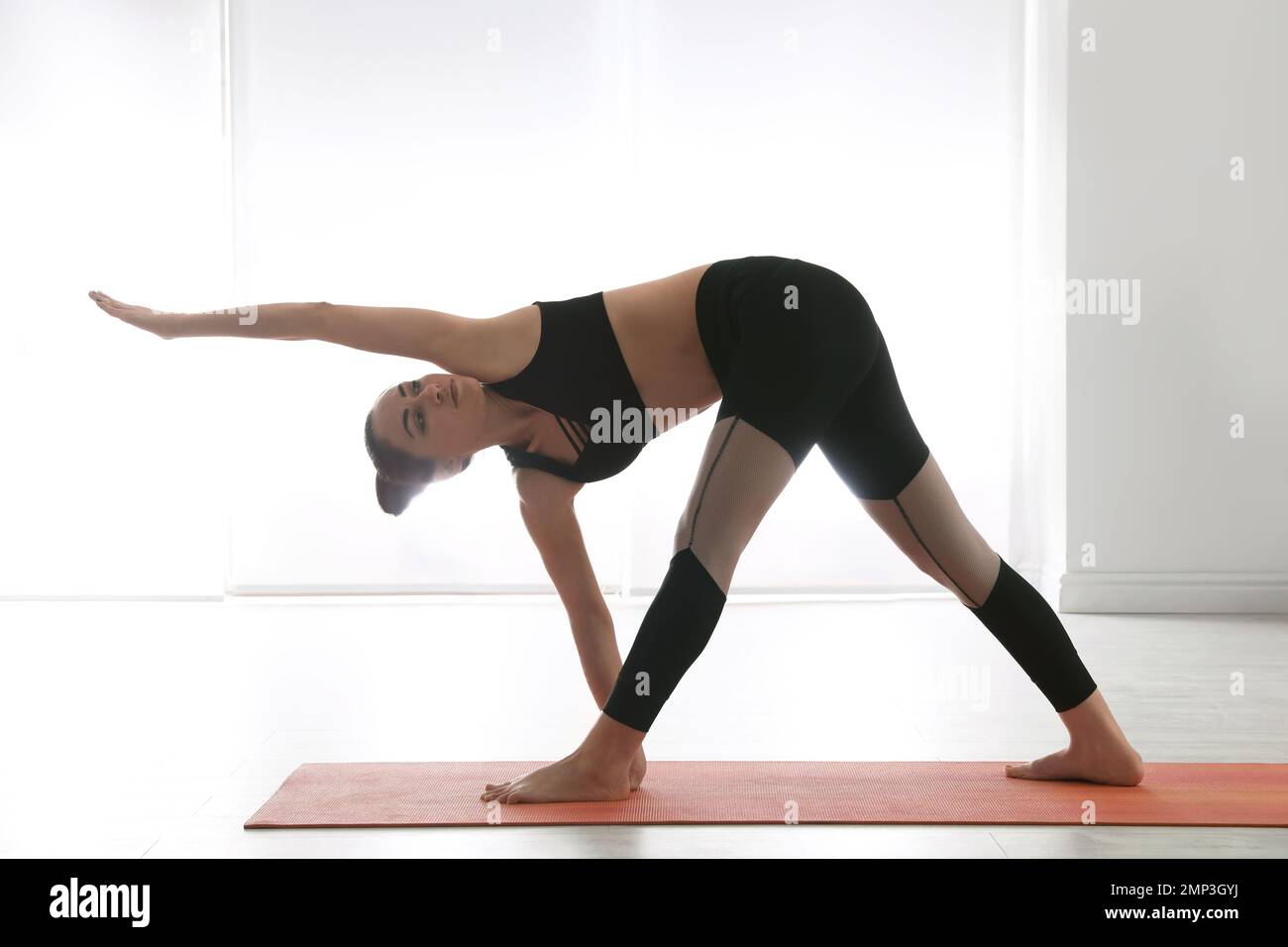 Young woman practicing extended triangle asana in yoga studio. Utthita ...