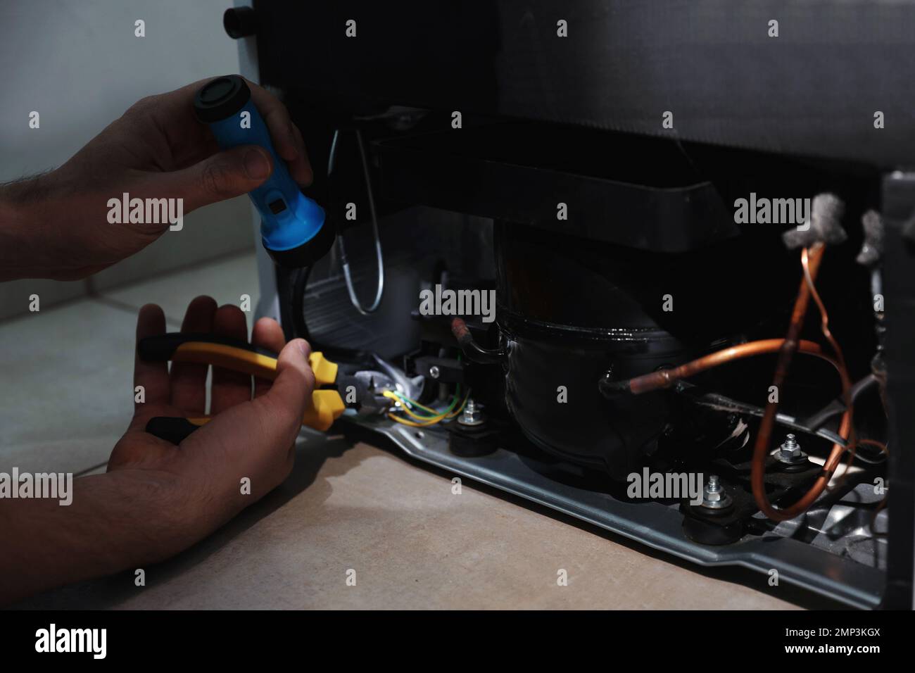 Man with flashlight fixing refrigerator indoors, closeup Stock Photo ...