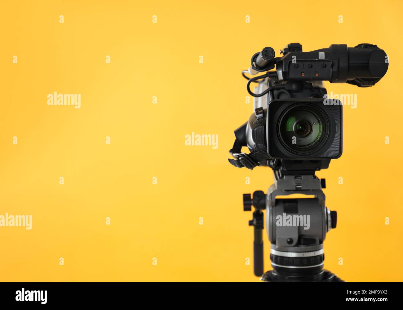 Modern professional video camera on yellow background. Space for text ...