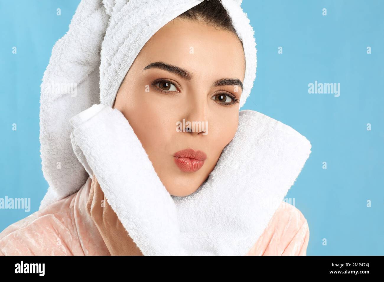 Young woman wiping face with towel on light blue background Stock Photo ...