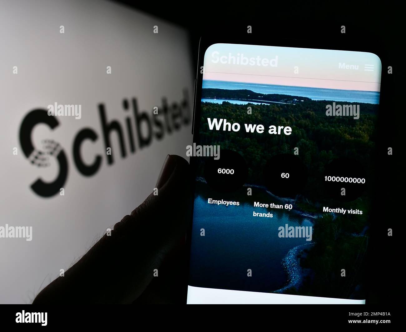 Person holding cellphone with website of Norwegian company Schibsted ...