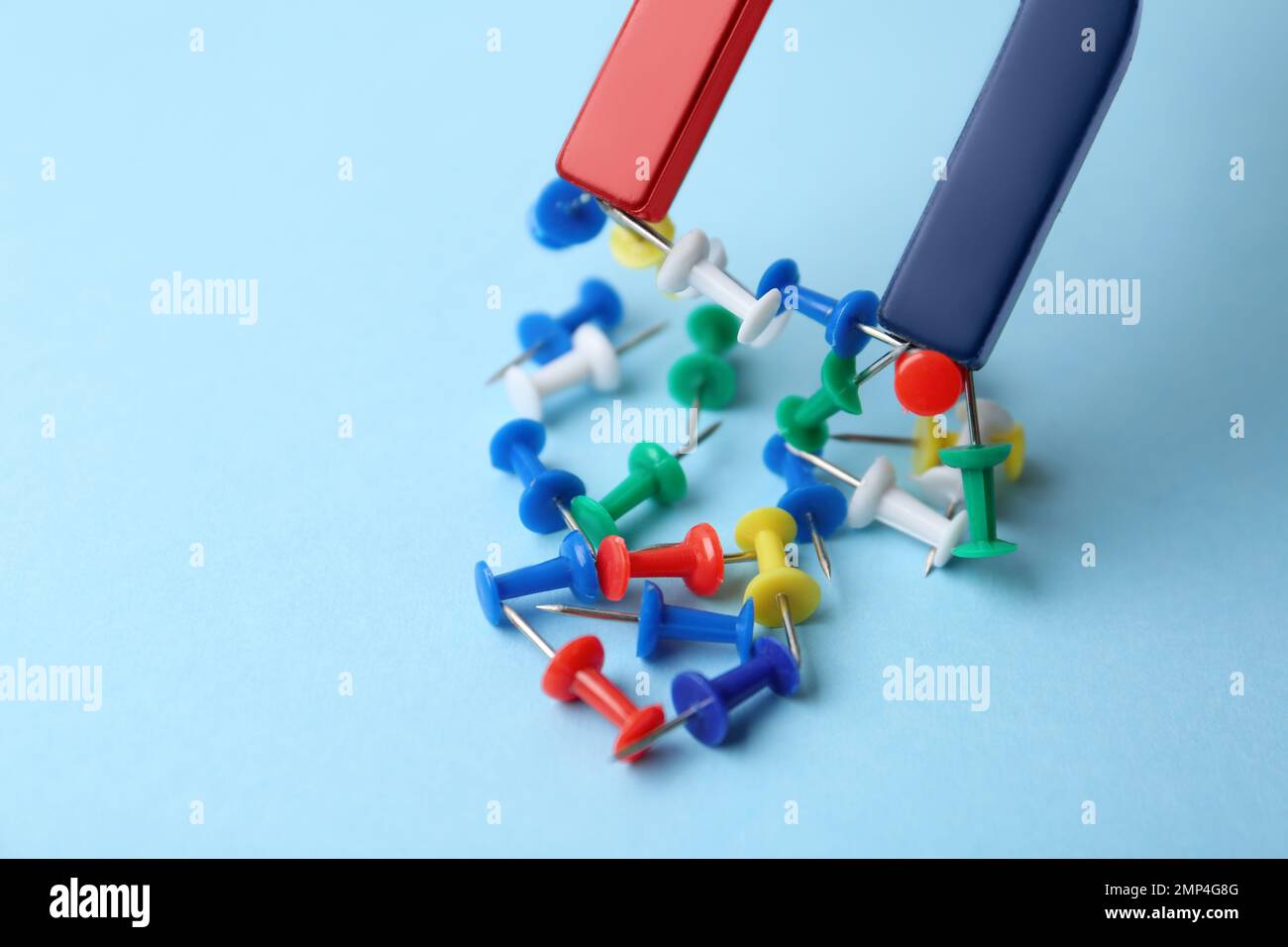 Magnet attracting colorful pins on light blue background, closeup Stock ...