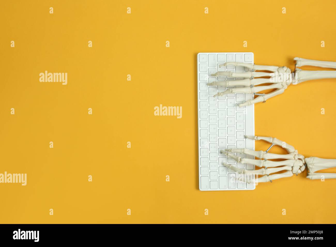 Human skeleton using computer keyboard on yellow background, top view ...