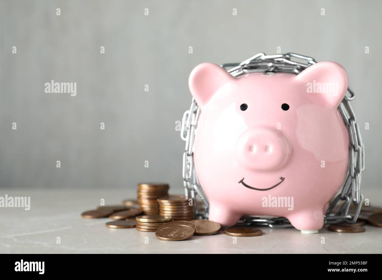 Piggy bank with steel chain and coins on grey marble table, space for ...