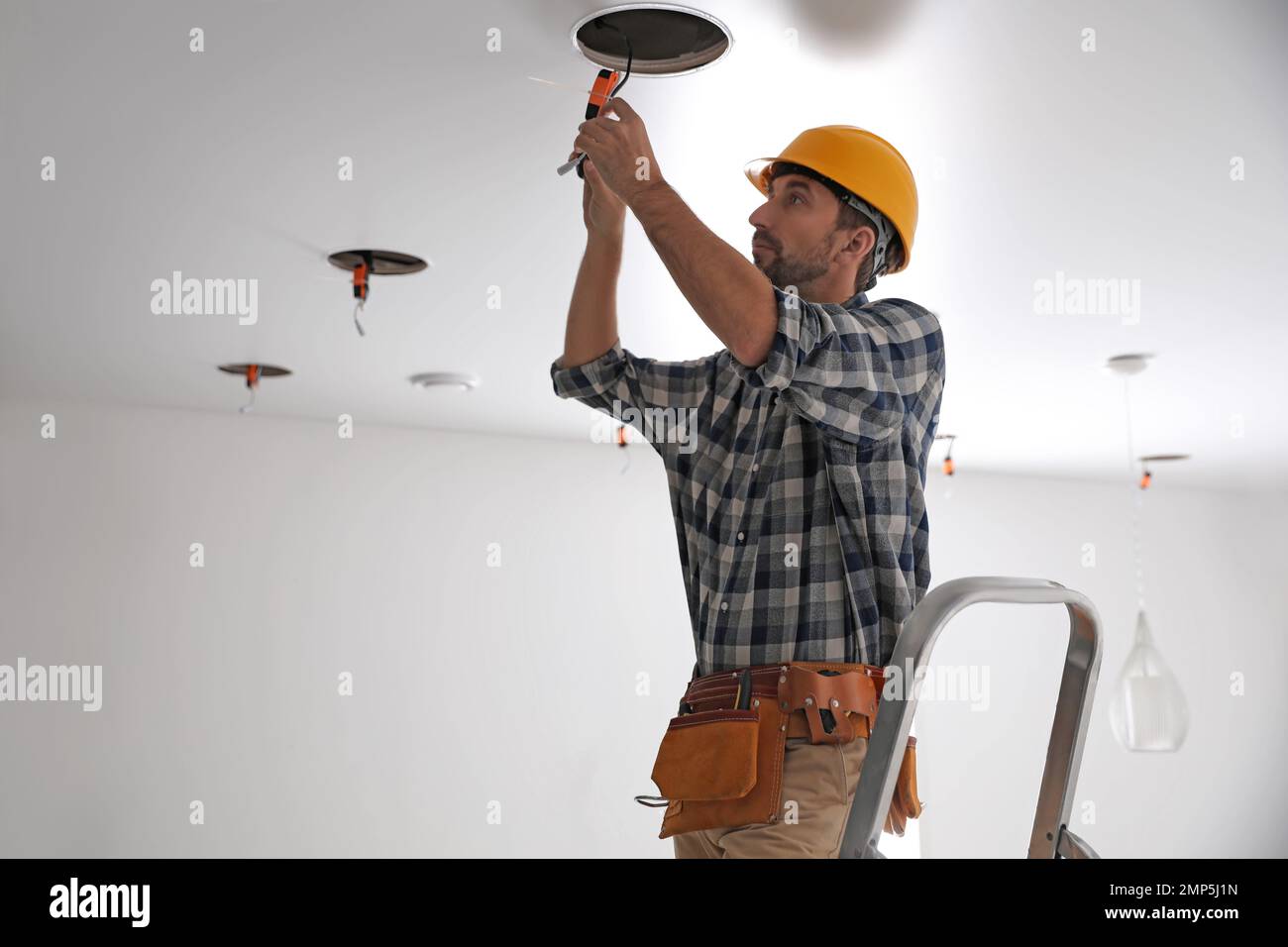 Worker installing lamp on stretch ceiling indoors Stock Photo - Alamy