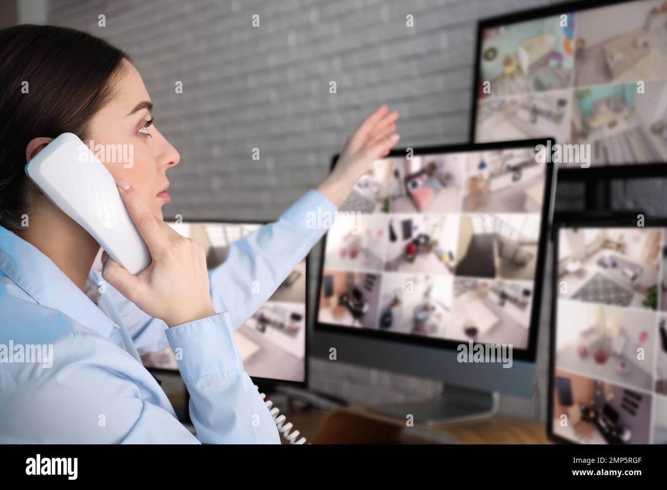 Female security guard talking by telephone near monitors at workplace ...