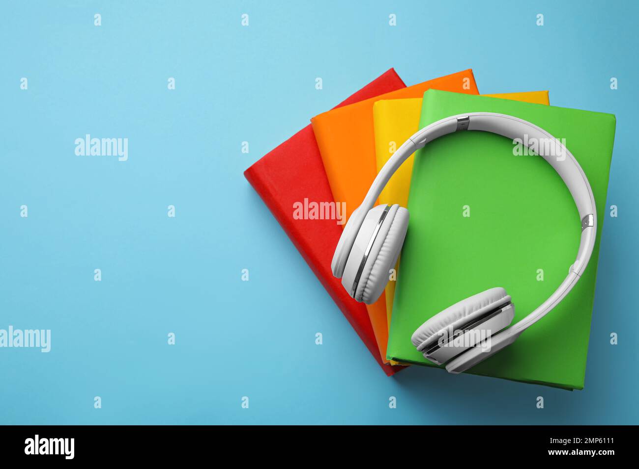 Books and modern headphones on light blue background, top view. Space ...