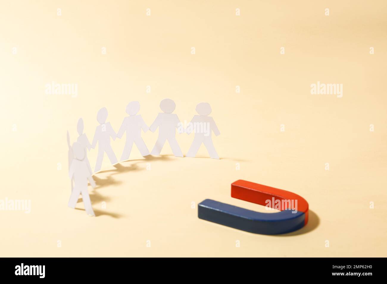Magnet attracting paper people on beige background Stock Photo - Alamy