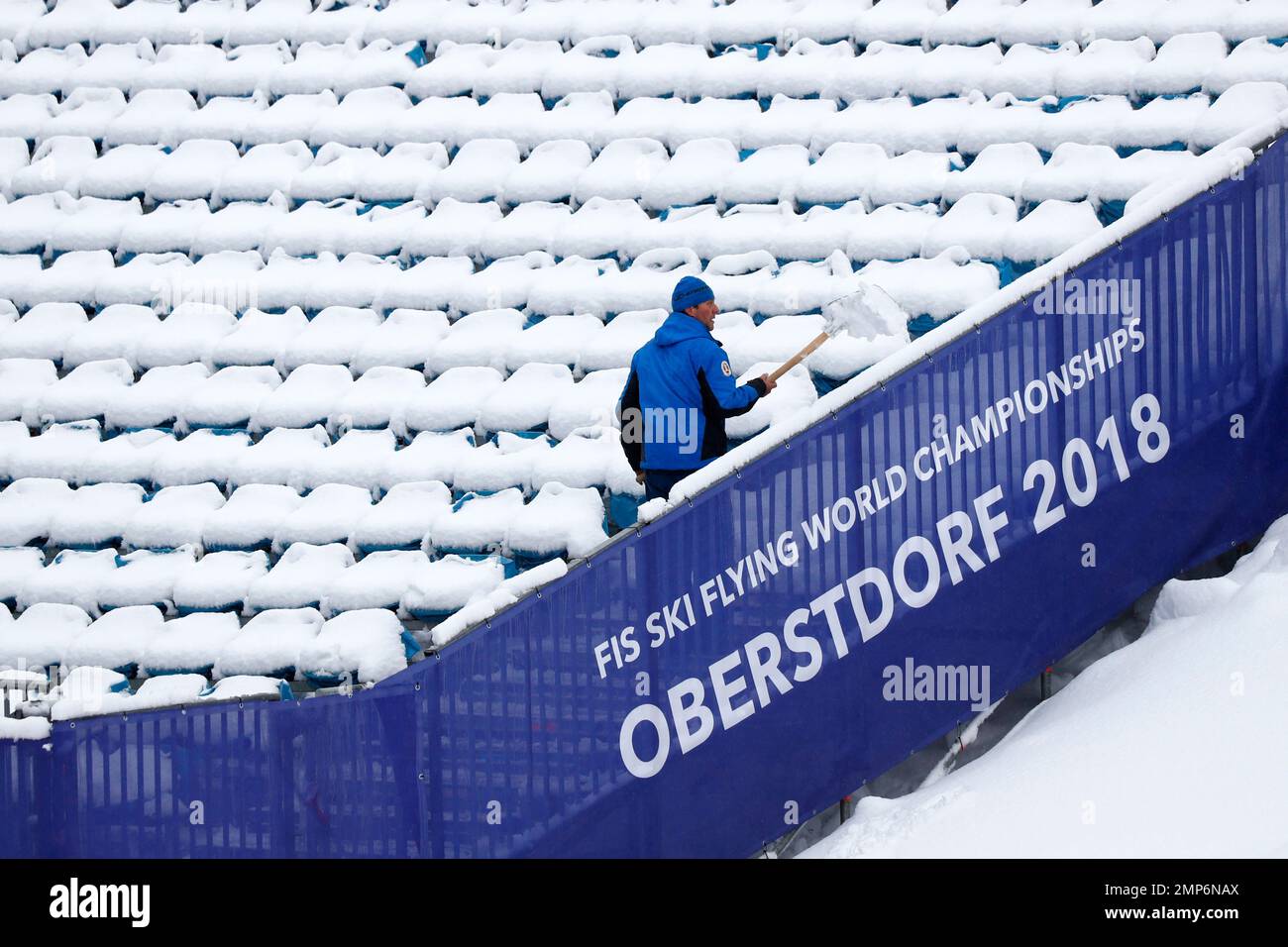A volunteer clears snow from spectator seats in the Ski Jumping stadium ...