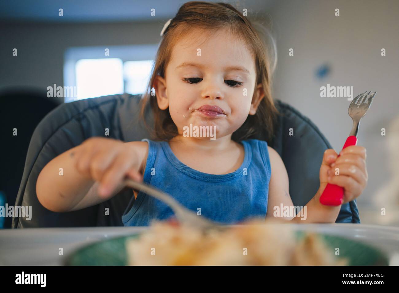 Little girl eating with two forks while sitting in a highchair. First ...