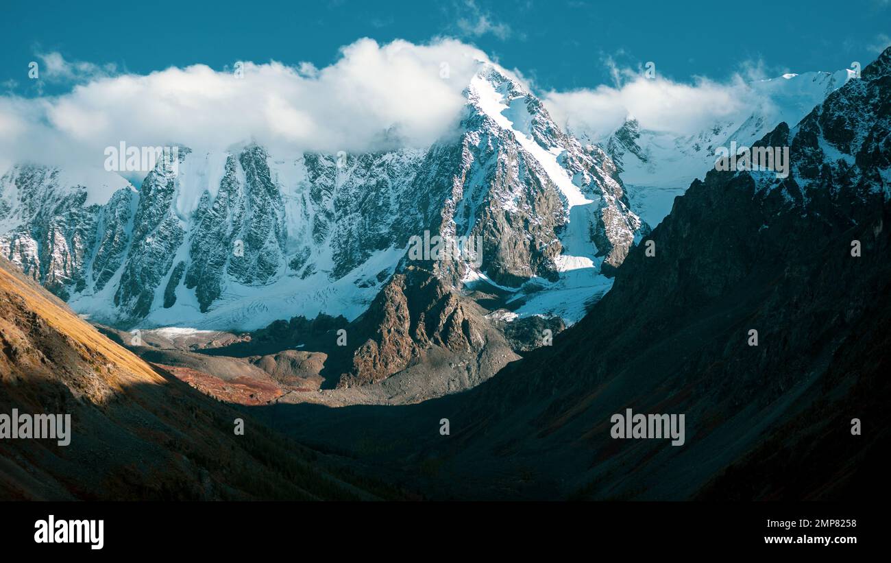 White clouds cover the tops of high rocky mountains with snow and ...