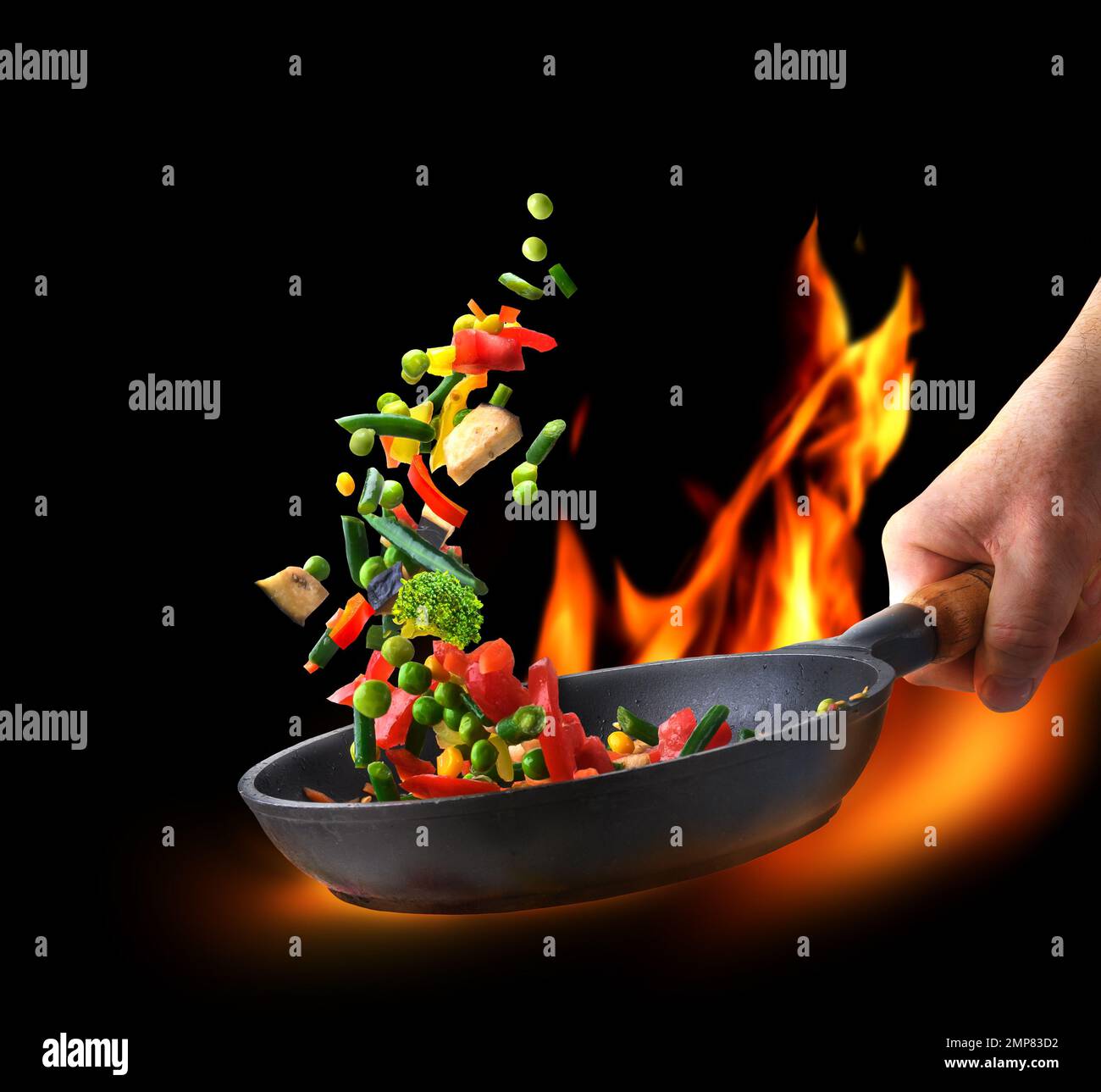 Fresh vegetables in a pan in chef hand on fire and black background ...
