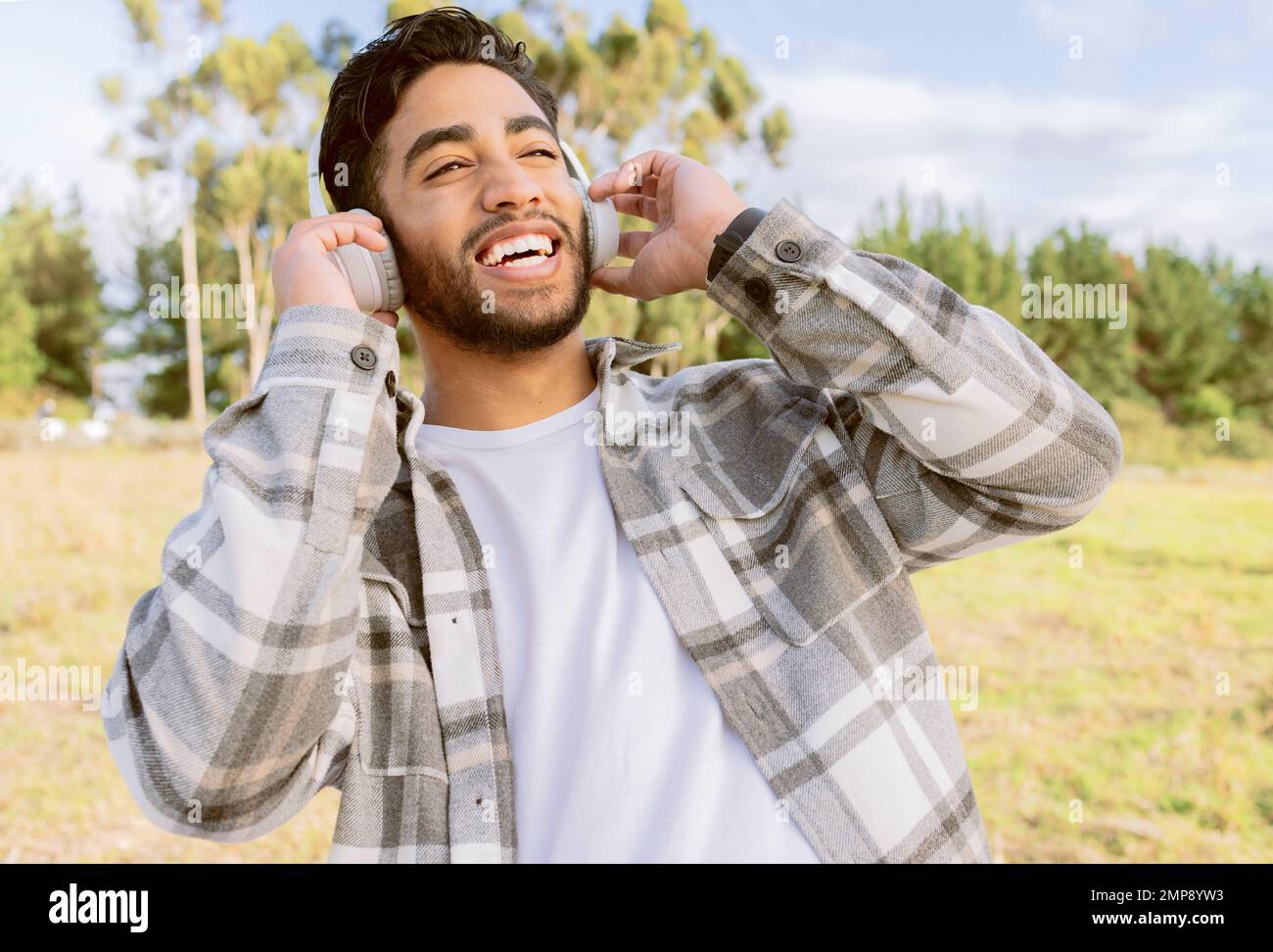 Happy, man and music with headphones in forest, laugh and relax on blue ...