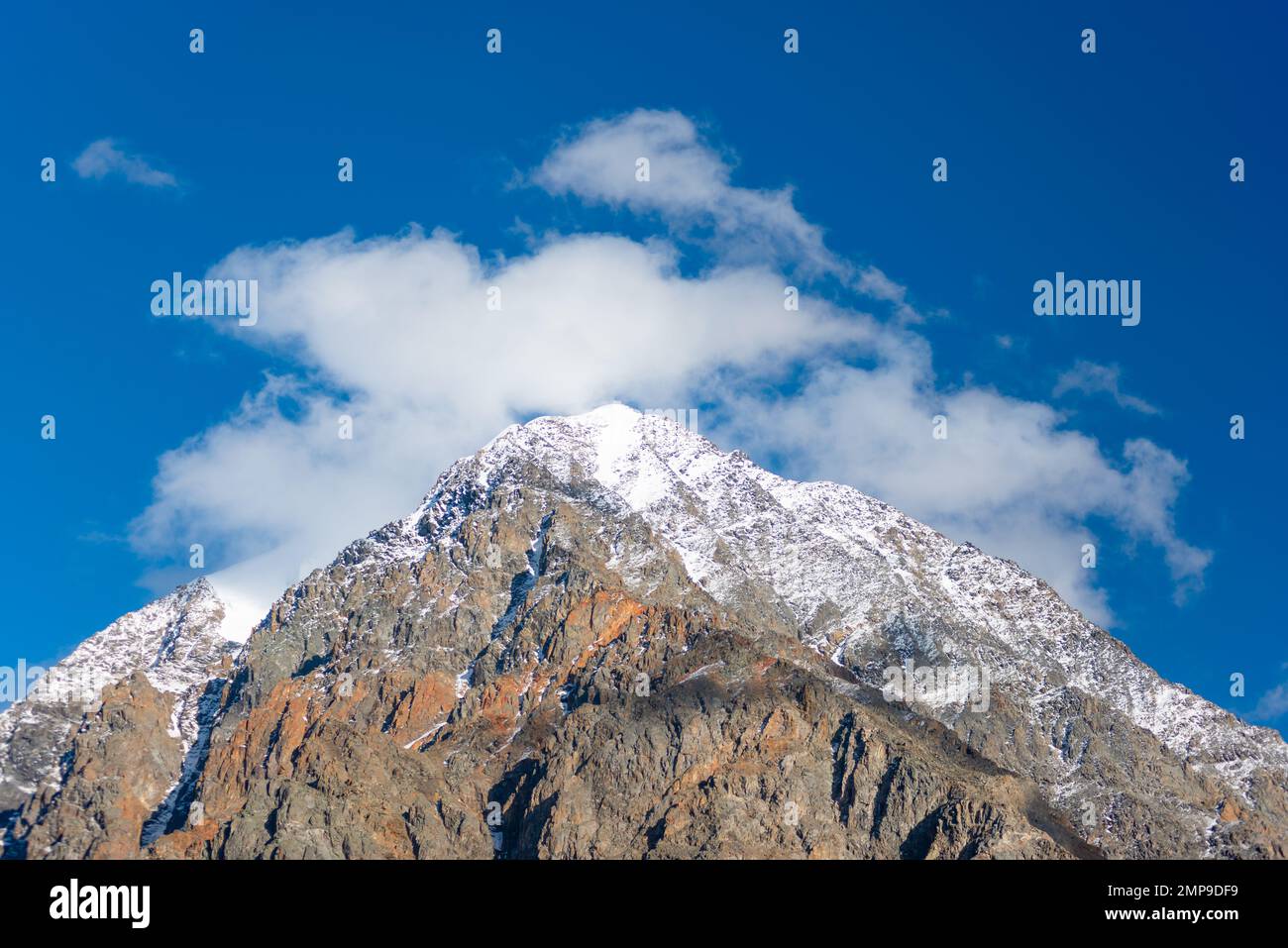 The top of a triangular rocky mountain is covered with snow against the ...