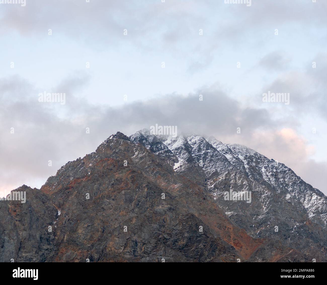 The top of a triangular rocky mountain is covered with snow against the ...