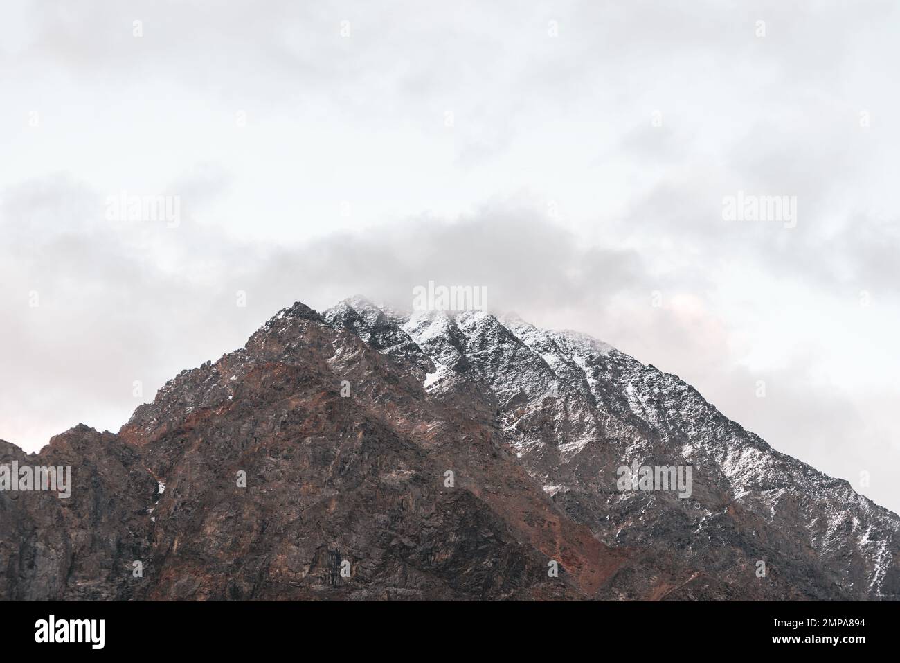 The top of a triangular rocky mountain is covered with snow against the ...