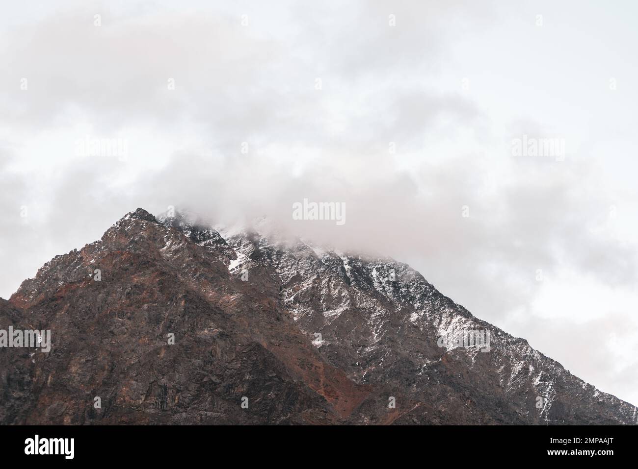 The top of a triangular rocky mountain is covered with snow against the ...