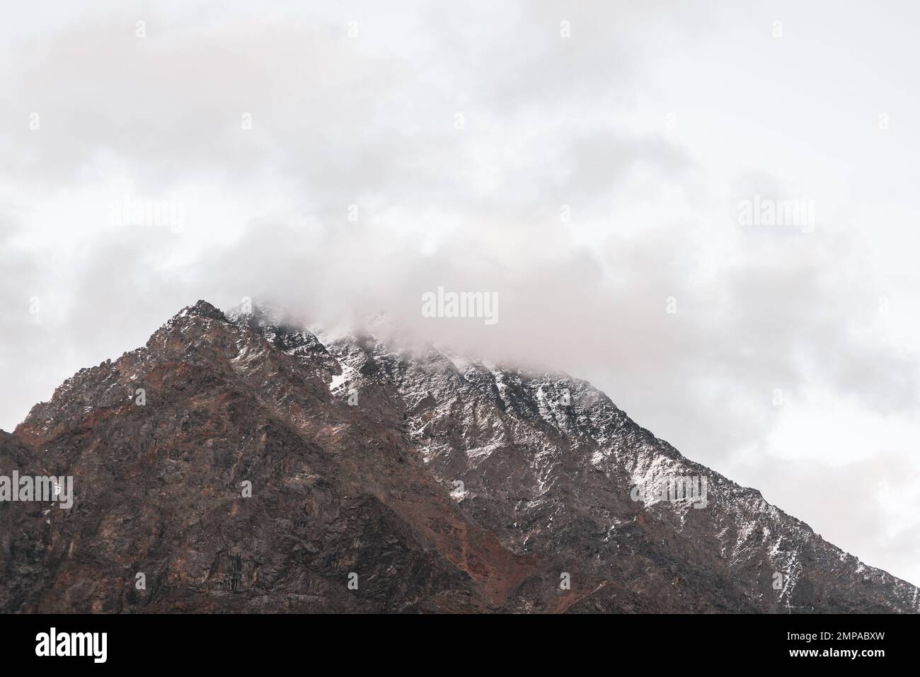 The top of a triangular rocky mountain is covered with snow against the ...