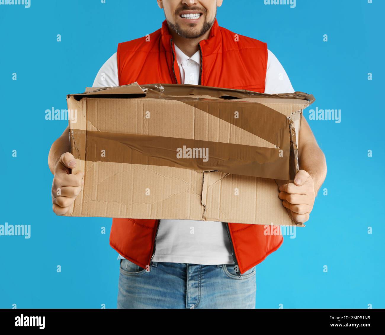 Emotional courier with damaged cardboard box on blue background ...