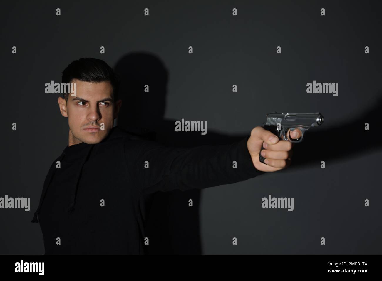 Professional killer with gun on black background Stock Photo - Alamy