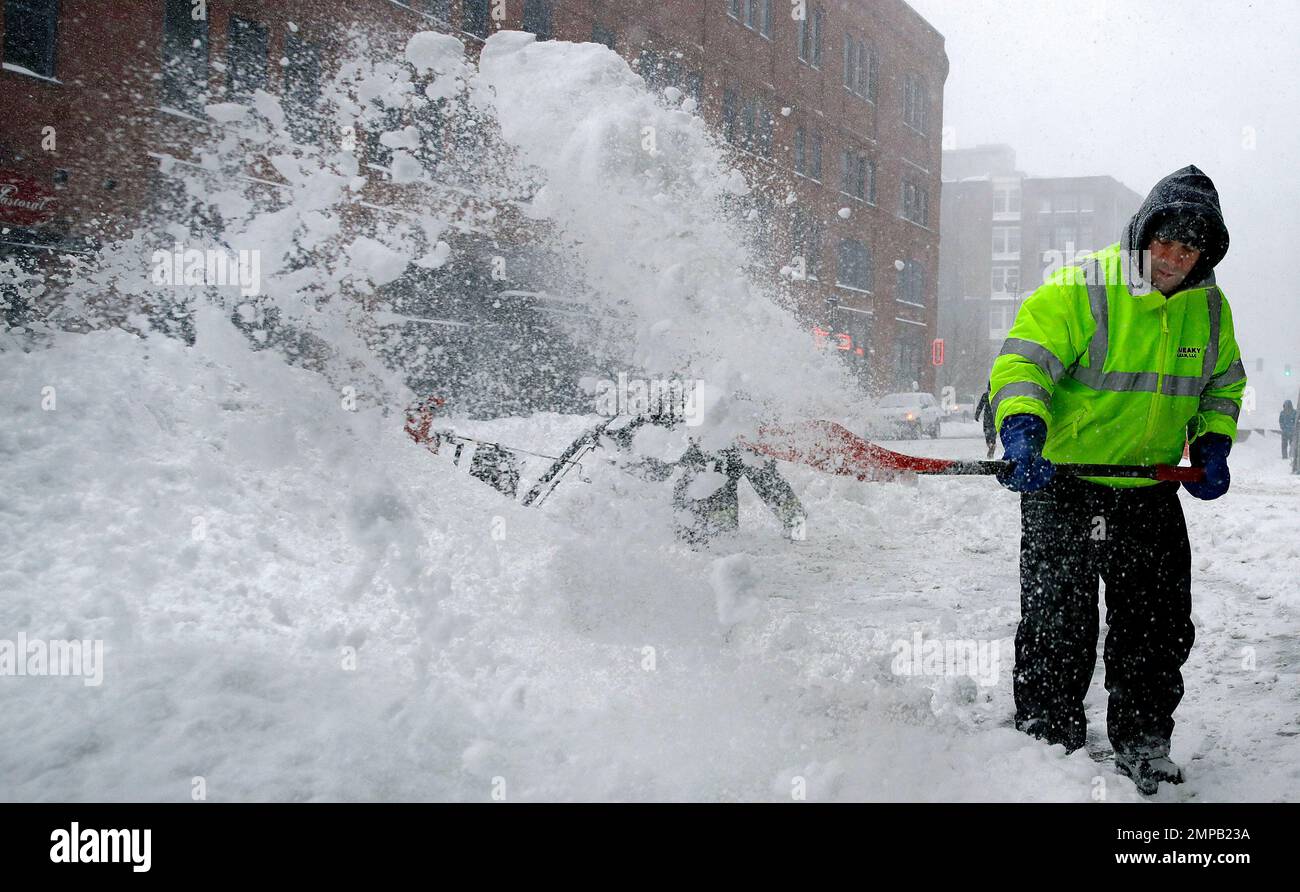 Workers clear snow from a sidewalk in the Seaport District of Boston ...