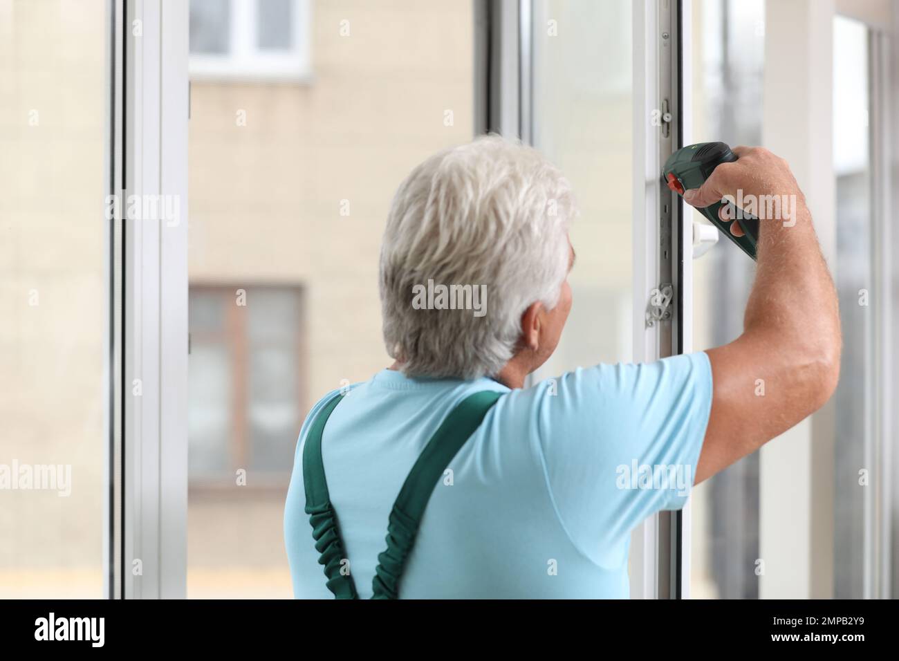Mature construction worker repairing plastic window with electric ...