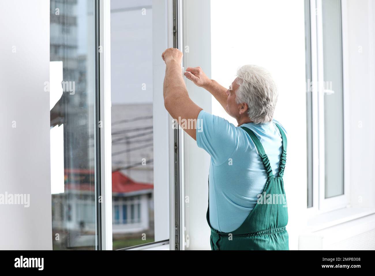 Mature construction worker repairing plastic window indoors Stock Photo ...