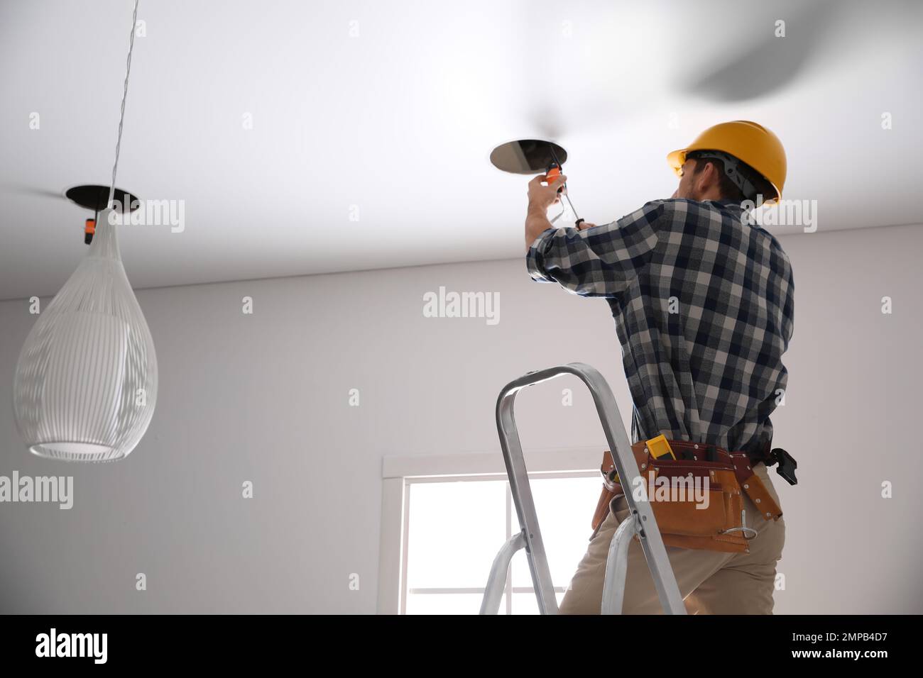 Worker installing lamp on stretch ceiling indoors. Space for text Stock ...