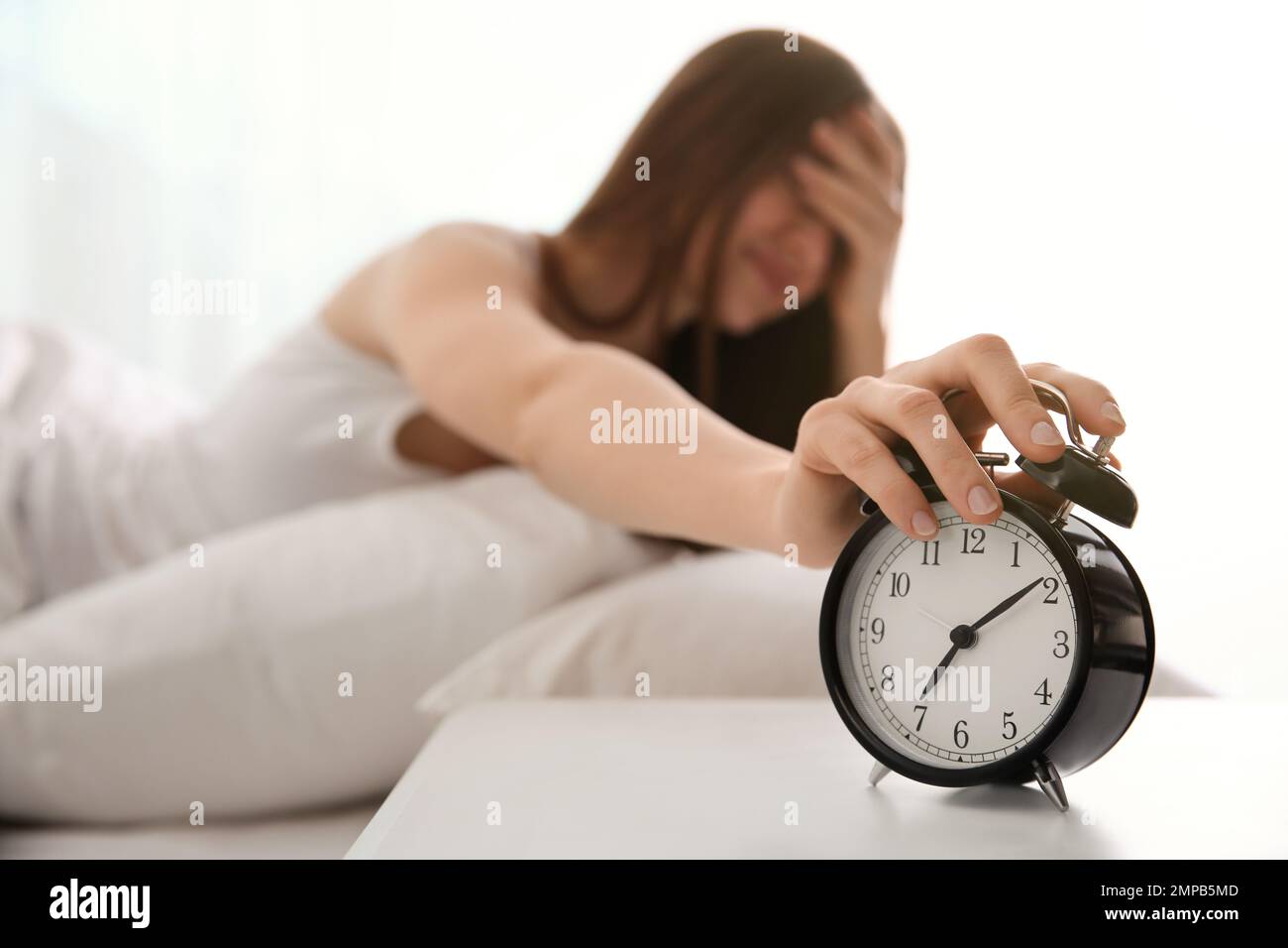 Young woman turning off alarm clock at home in morning, focus on hand ...