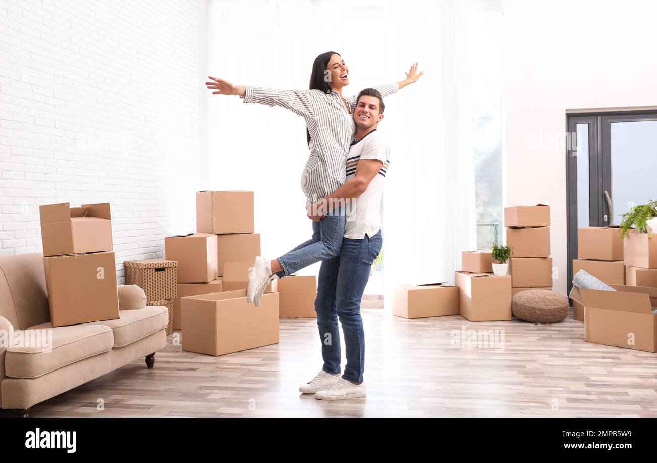 Happy couple having fun in room with cardboard boxes on moving day ...
