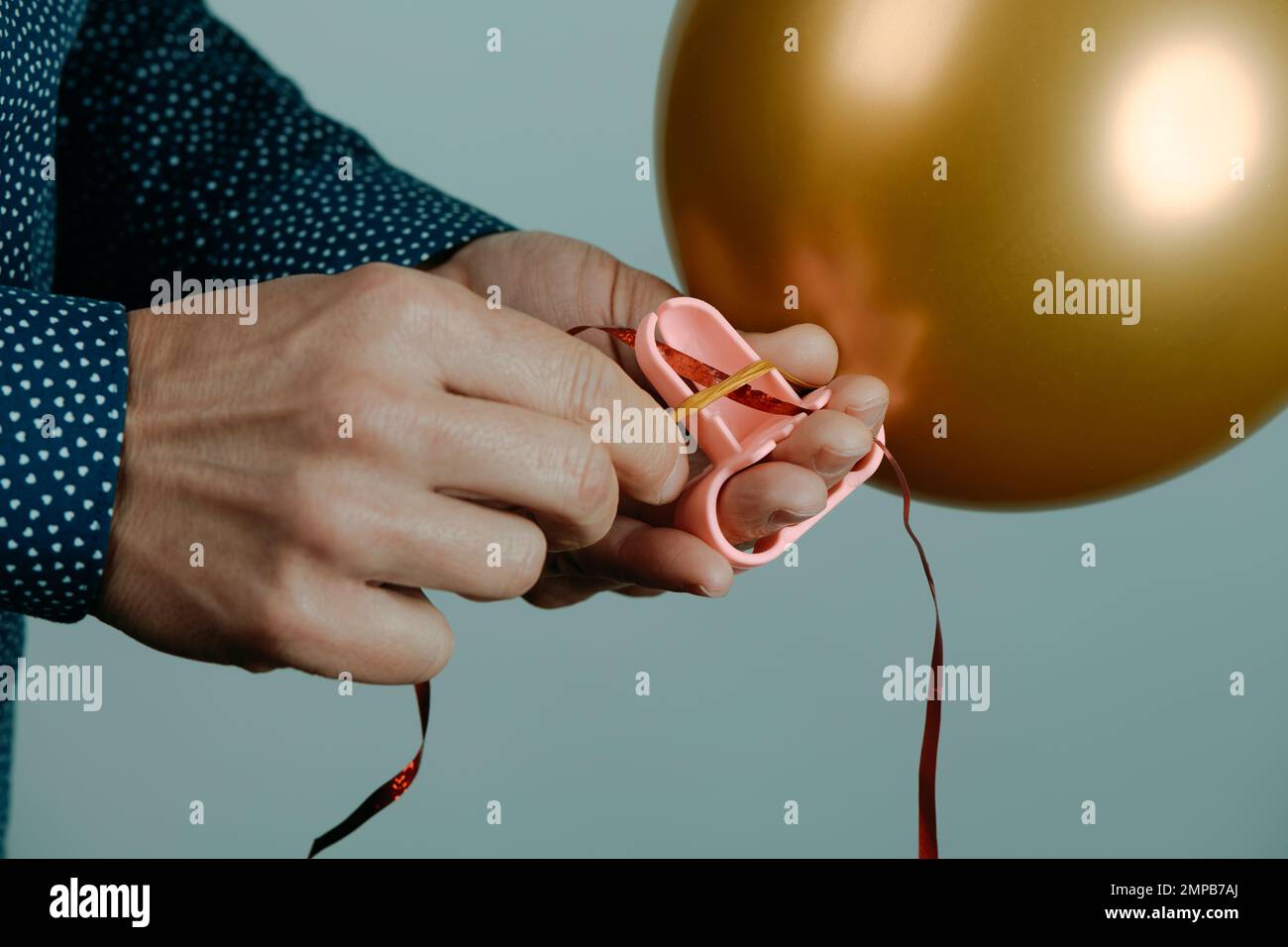 closeup of a man using a tool to tie an inflated golden balloon to a ...