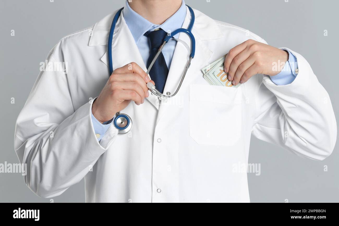 Doctor putting bribe into pocket on grey background, closeup ...