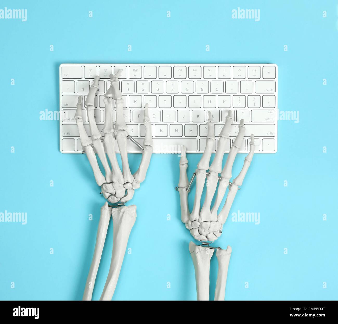 Human skeleton using computer keyboard on light blue background, top ...