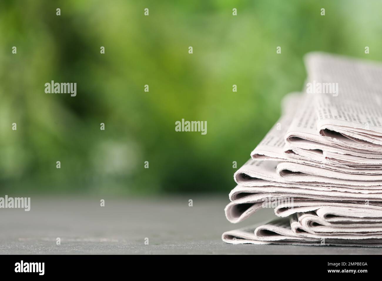 Stack of newspapers on grey table against blurred green background ...