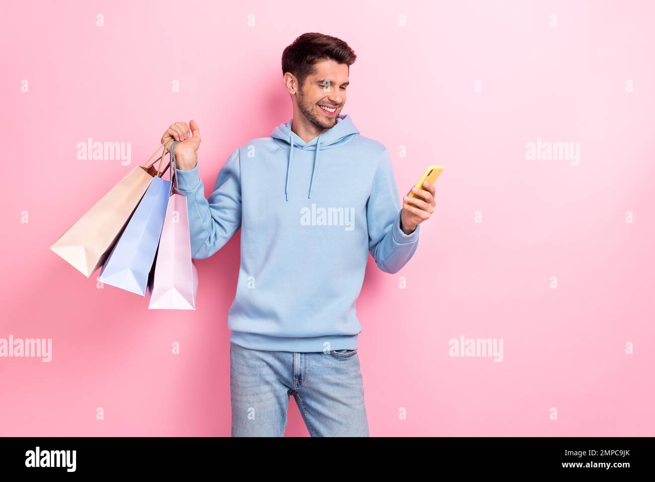 Photo of cool cheerful man wear blue hoodie holding bargains typing sms ...
