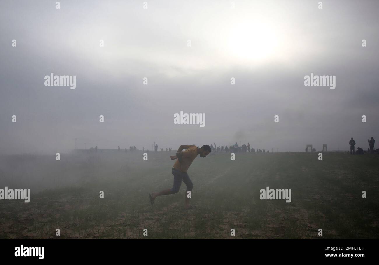 A Palestinian protester runs for cover from teargas fired by Israeli ...