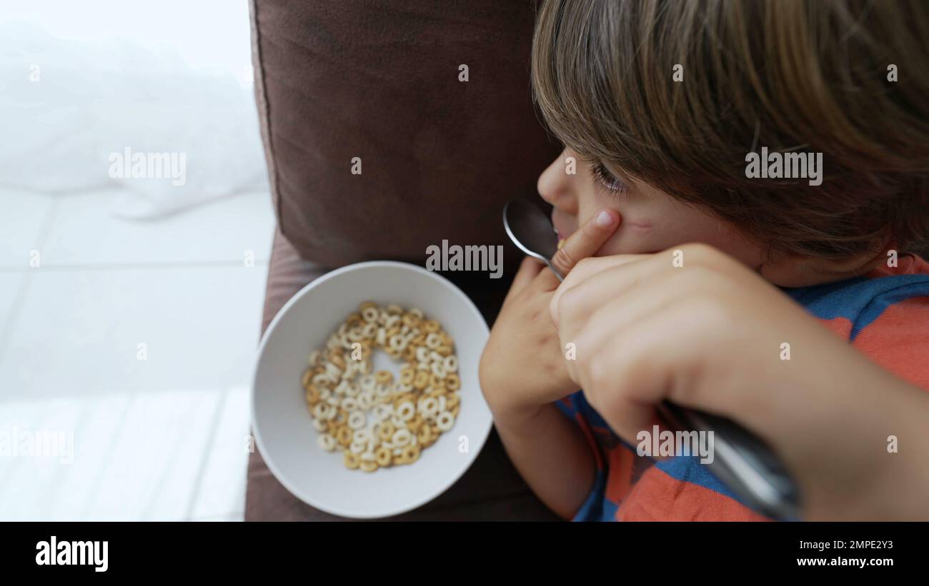 Child eating cereal lying on couch. One little boy eats morning food ...