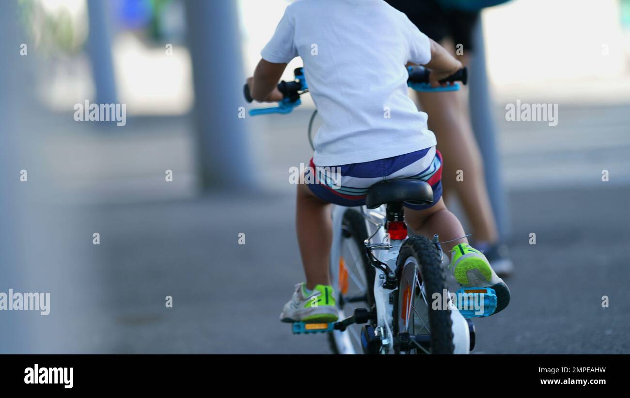 Back of child cyclist rides bike in street. Sportive kid riding bicycle ...